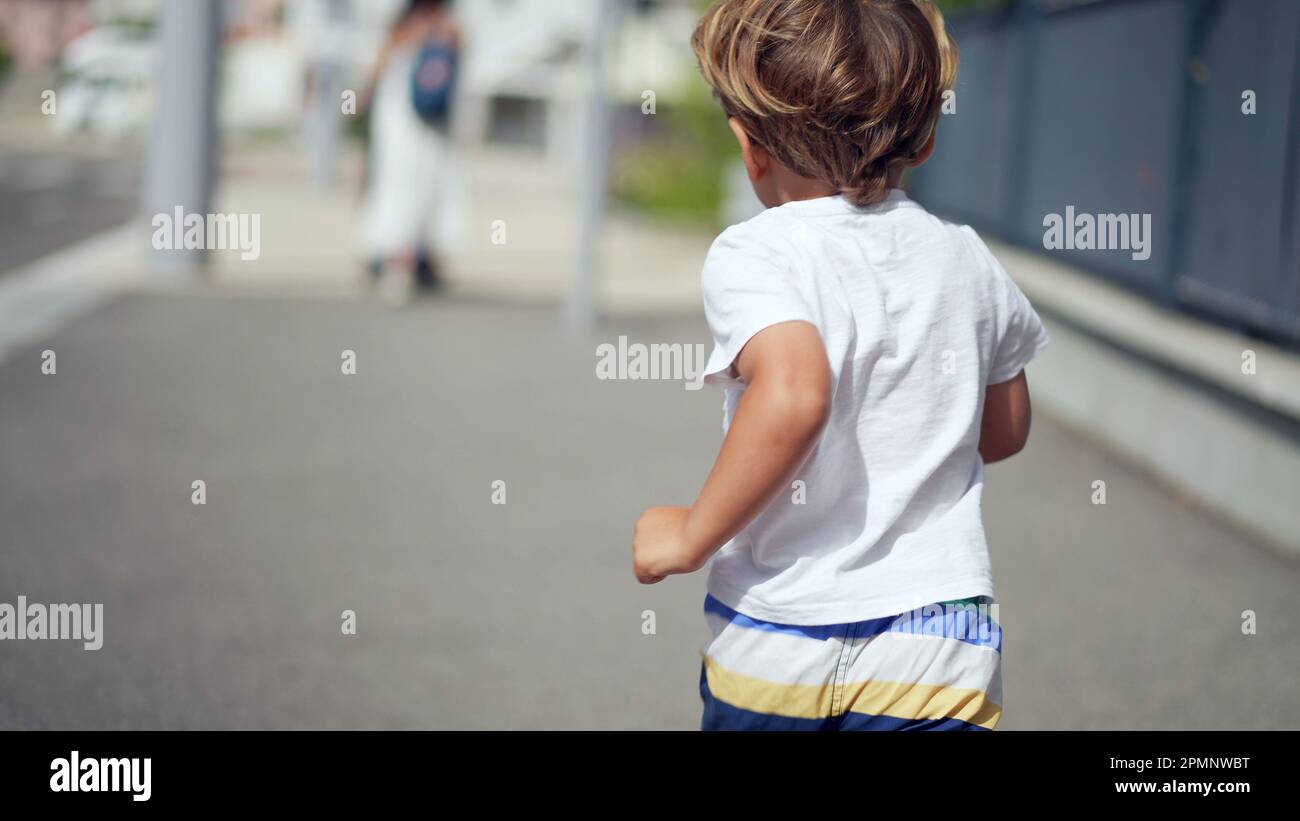 One joyful small boy running outdoors in city street sidewalk. Back of ...