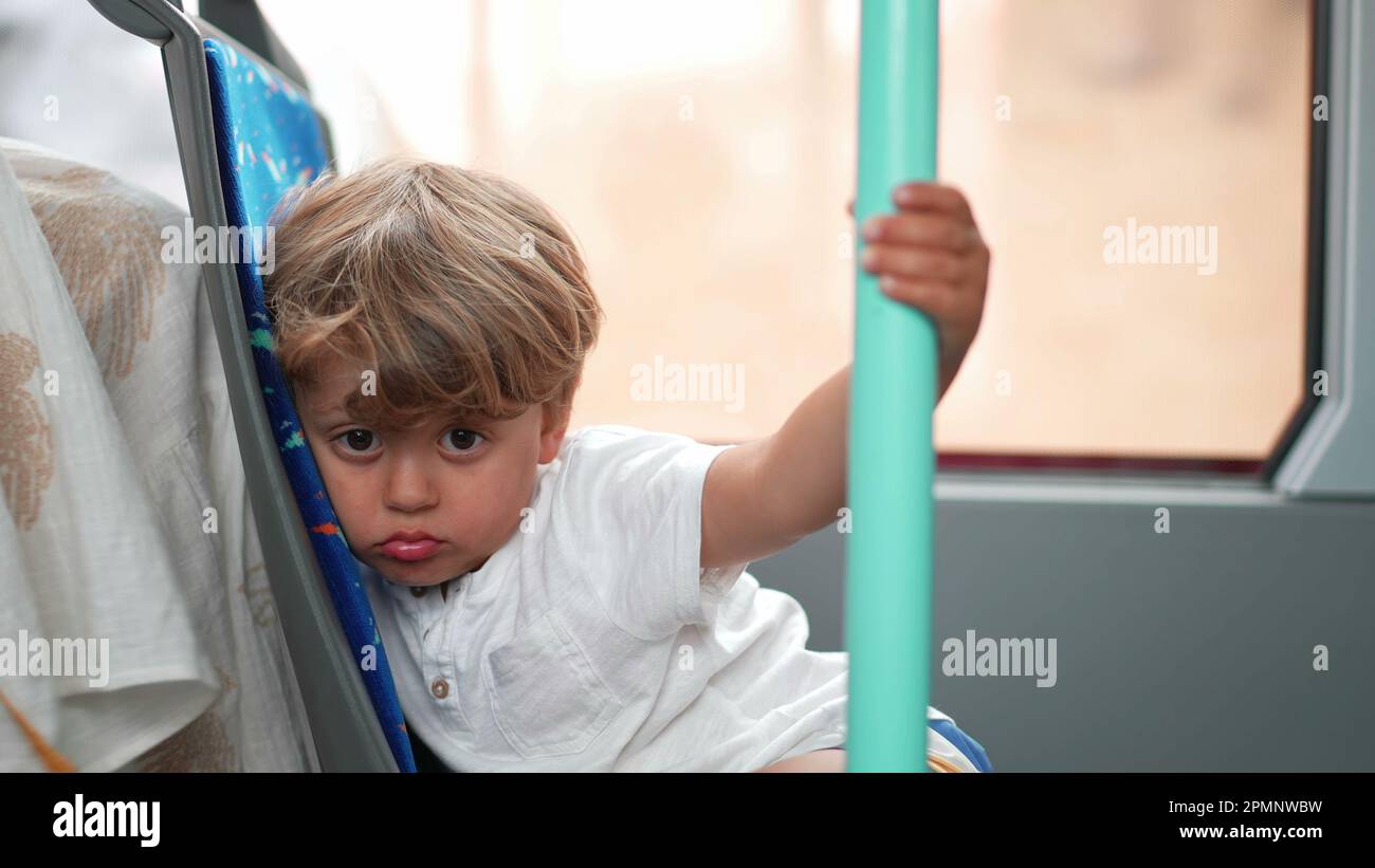 Sad child traveling by bus holding into metal bar pole. One passenger ...