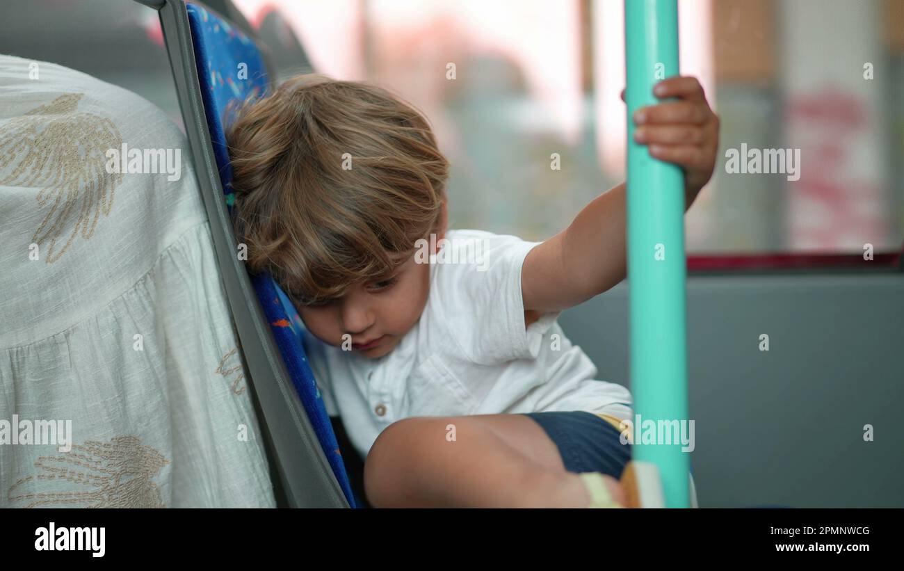 Sad child traveling by bus holding into metal bar pole. One passenger ...