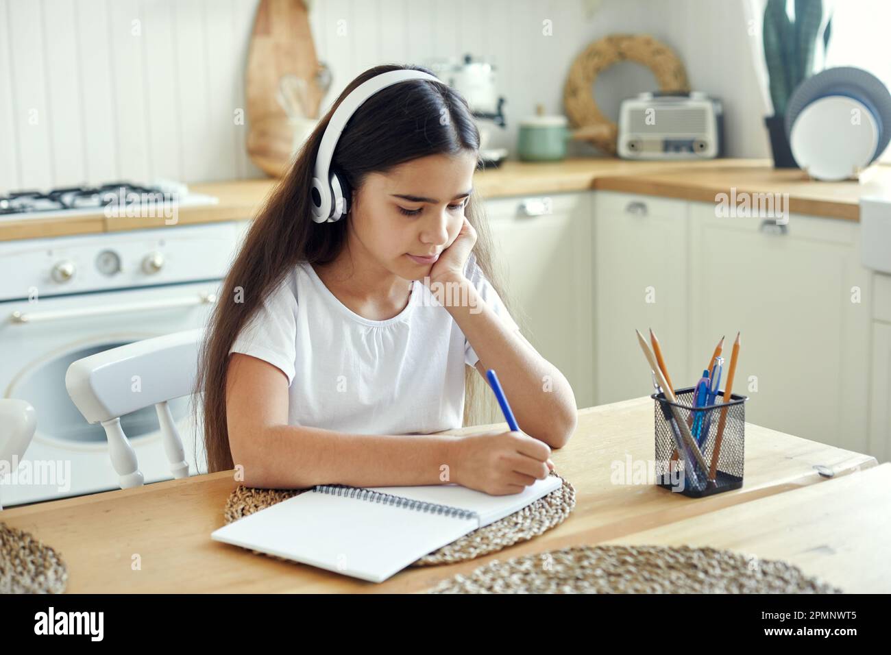 Pretty pre-teen girl in wireless headphones writing task, makes ...