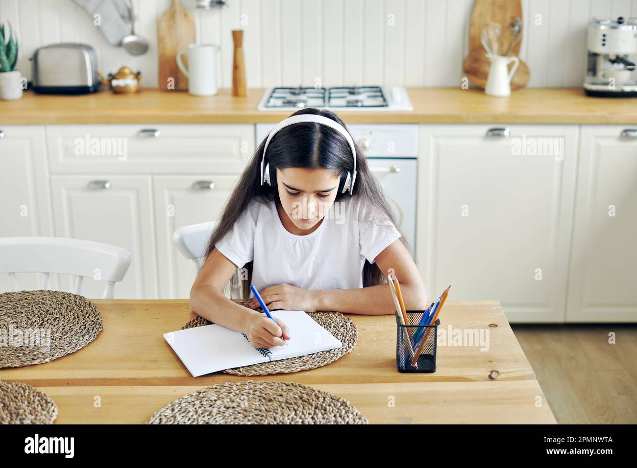 Pretty pre-teen girl in wireless headphones writing task, makes ...