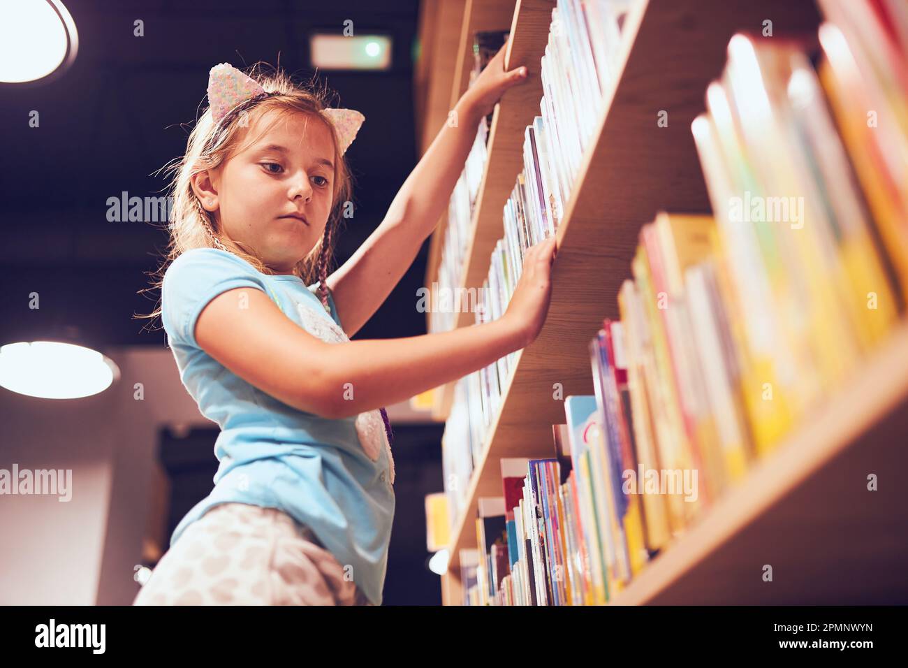 Schoolgirl looking for book in school library. Student choosing book ...