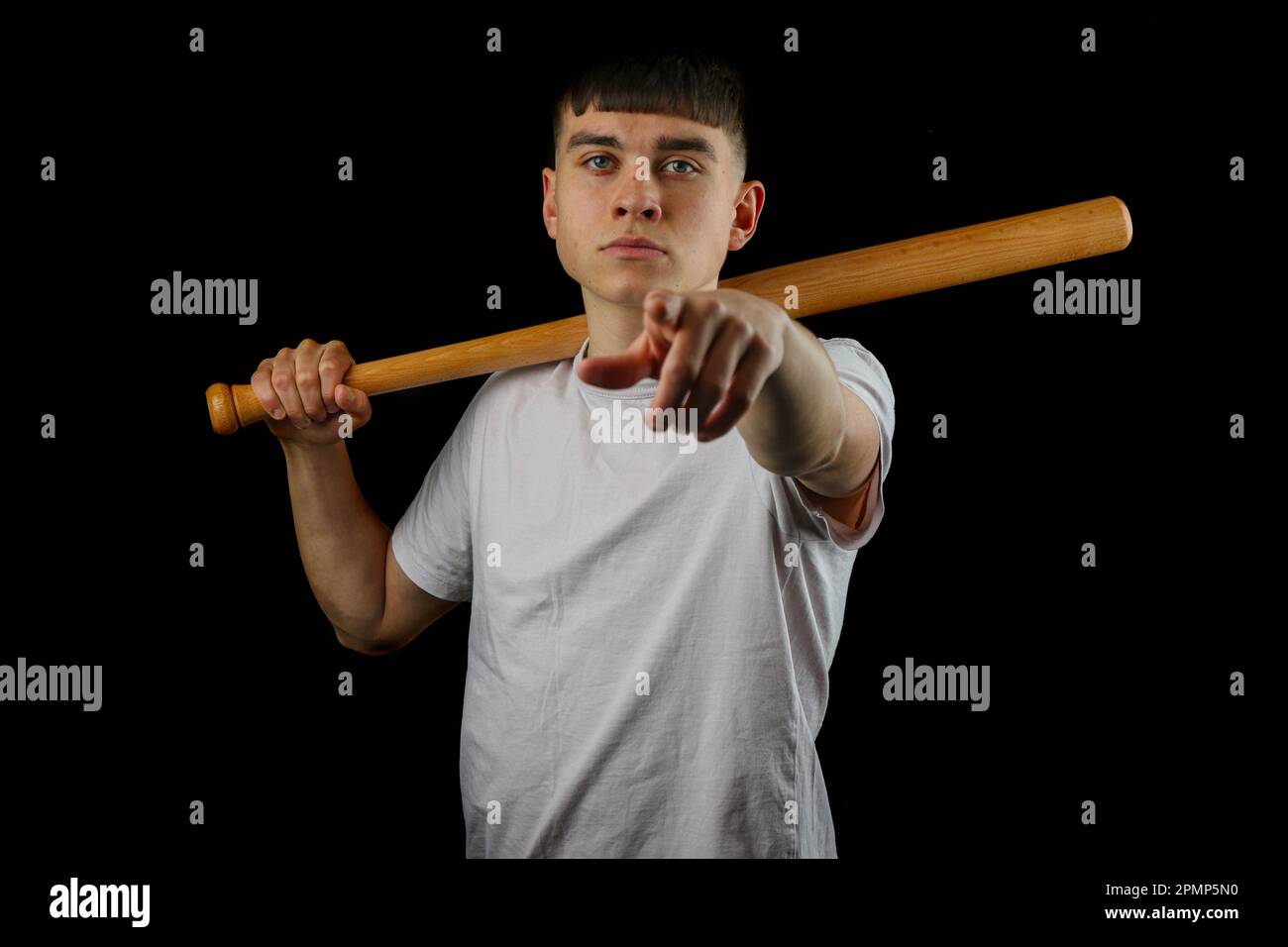 A teenage boy with a basball bat and pointing against a black ...