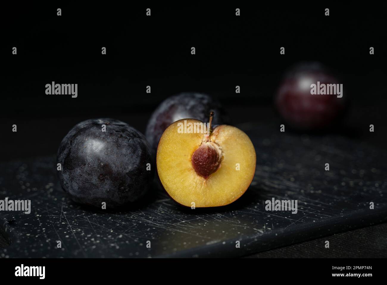 Cut plum showing an open half with fruitstone on a black countertop ...