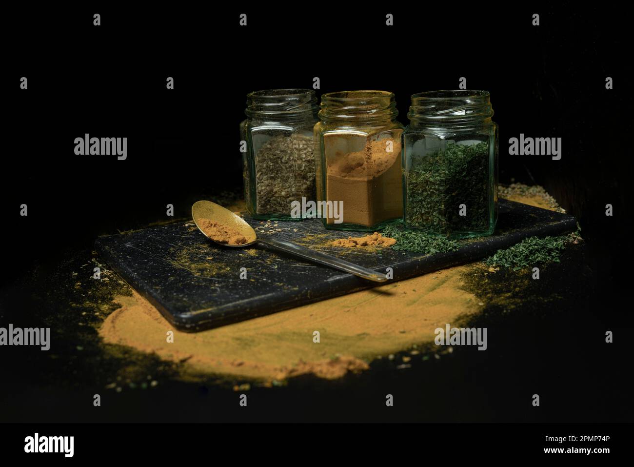 Three kinds of herbs or spices in glass jars sitting in a row on a ...
