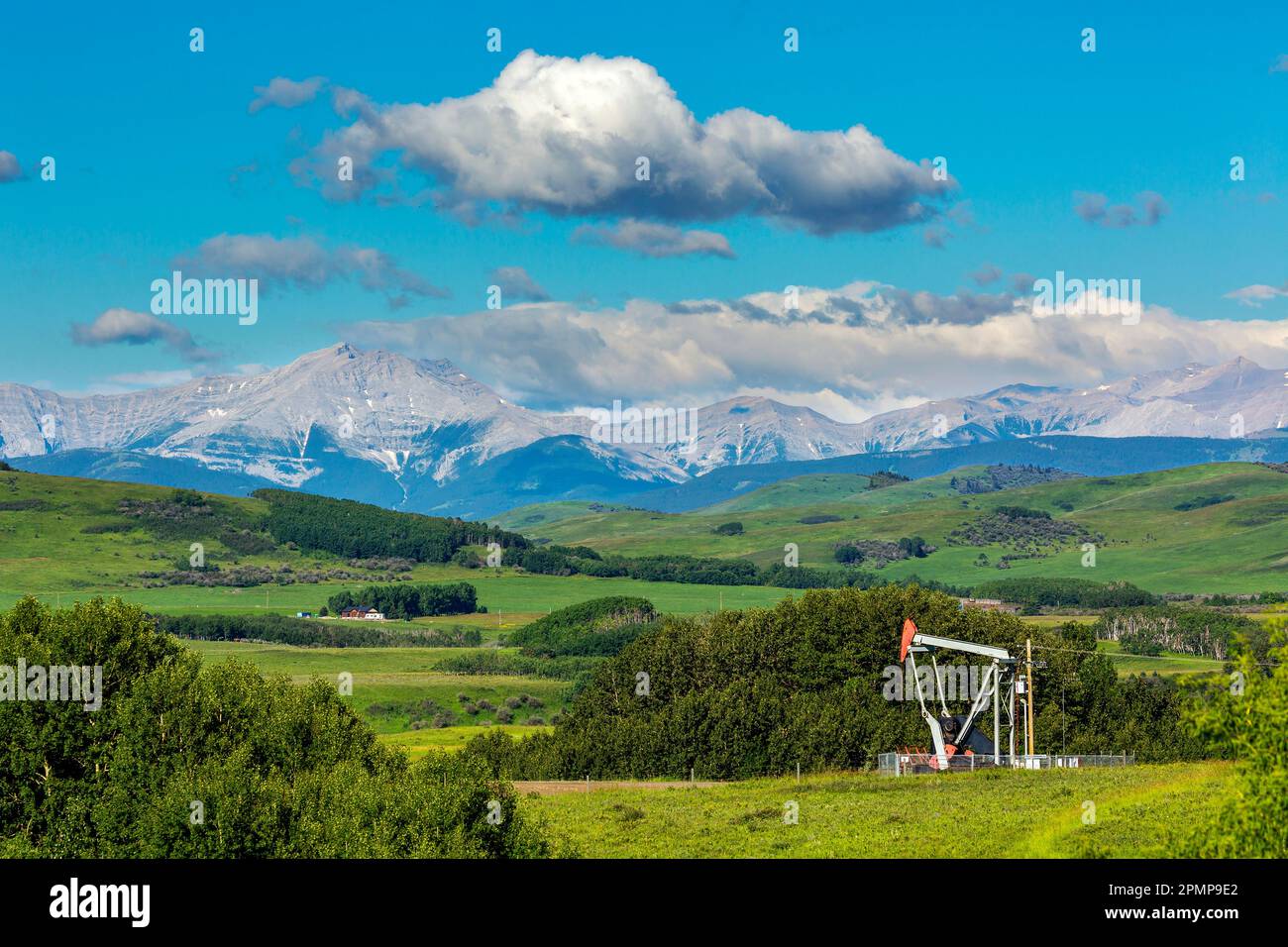 Pumpjack in a green field with trees, rolling hills, mountain range ...