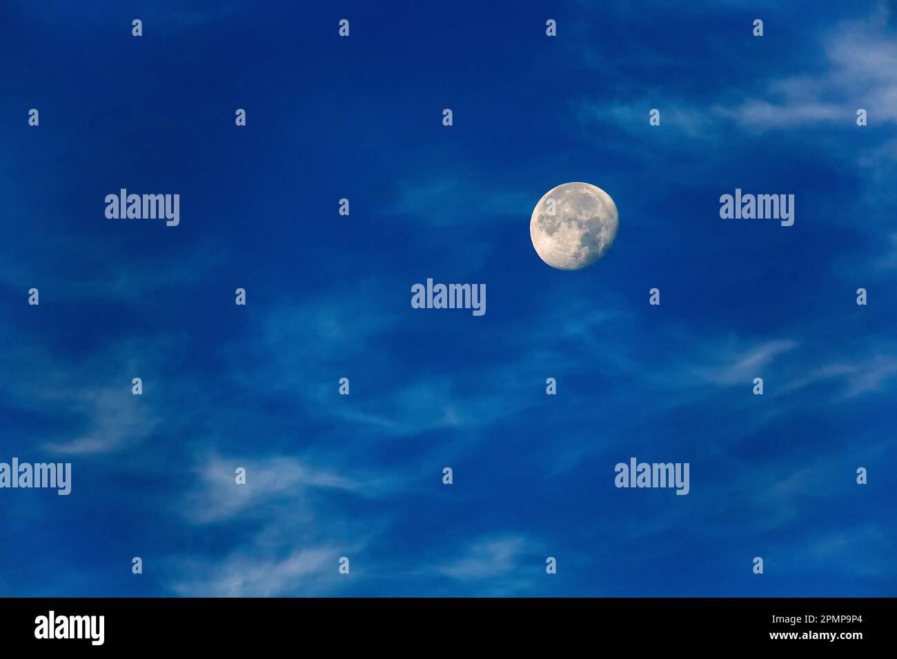 Mostly full moon in a blue sky with wispy clouds; Calgary, Alberta ...