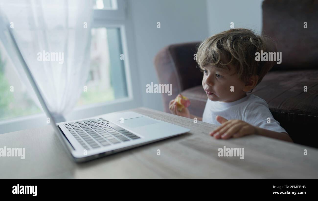 Child watching cartoons on laptop computer at home while eating apple ...