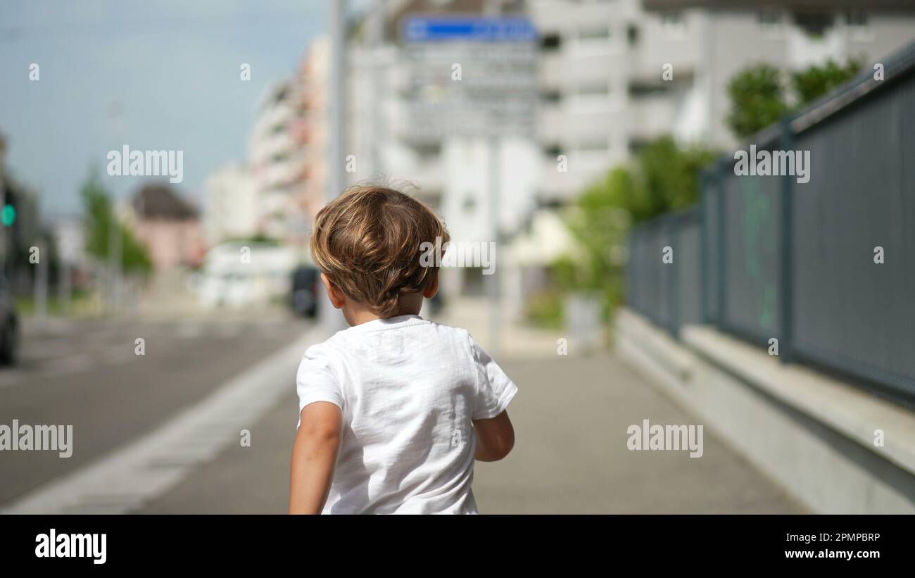 Back of happy active child running in city street sidewalk during sunny ...