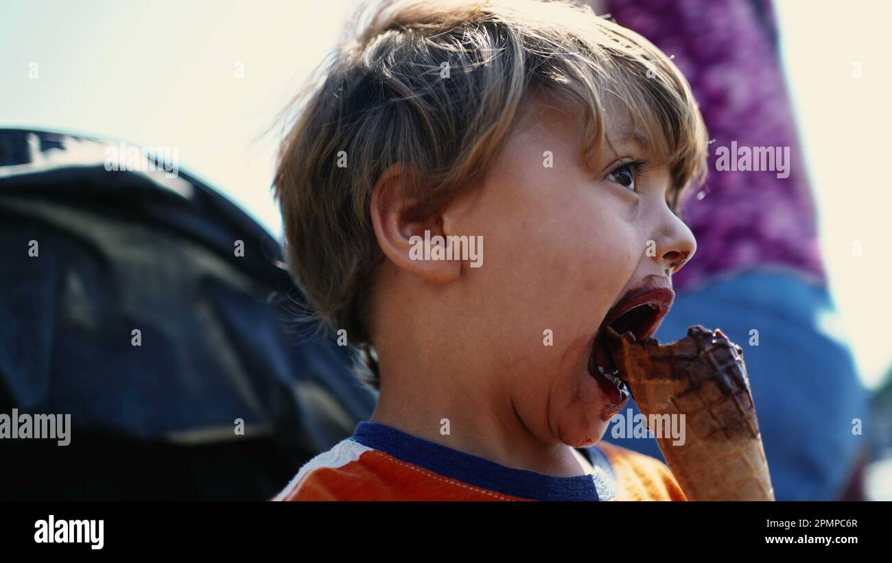 Small boy snacking chocolate icecream cone. Portrait face closeup of ...