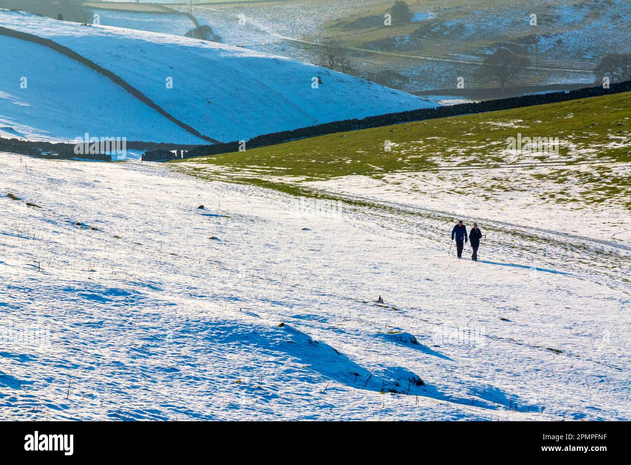Walkers hiking in a snow covered landscape with trees on the High Peak ...