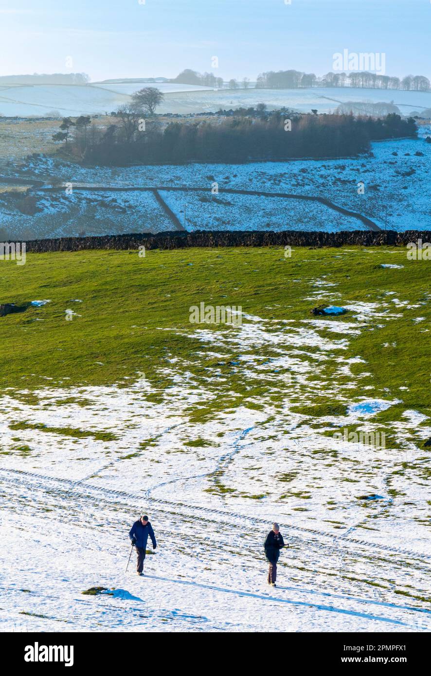 Walkers hiking in a snow covered landscape with trees on the High Peak ...