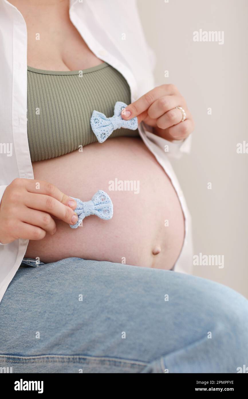 close up hands on pregnant mother holding baby clothes, two blue bows ...