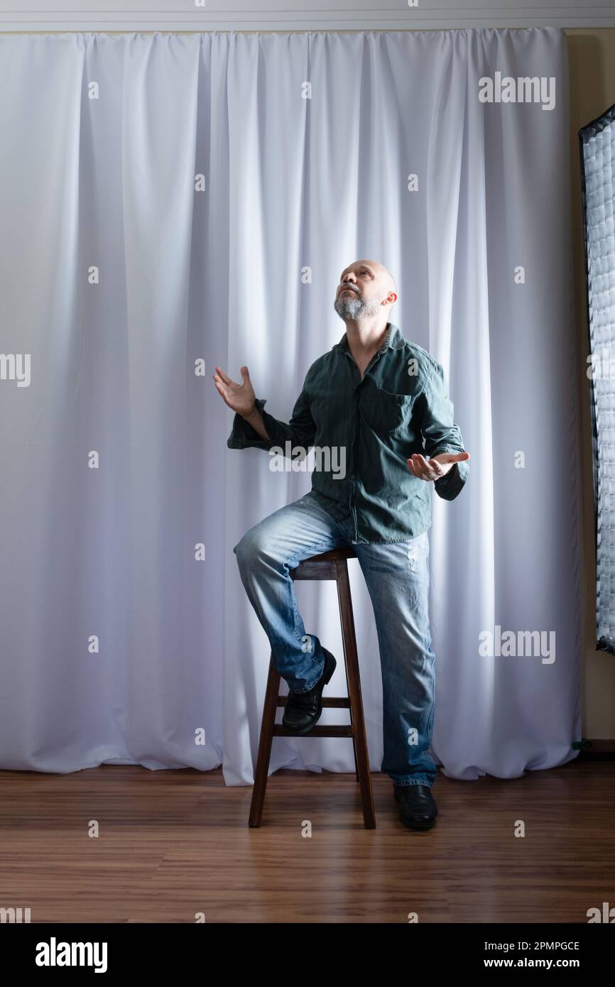 Studio portrait of a man sitting on a wooden stool. white curtain ...