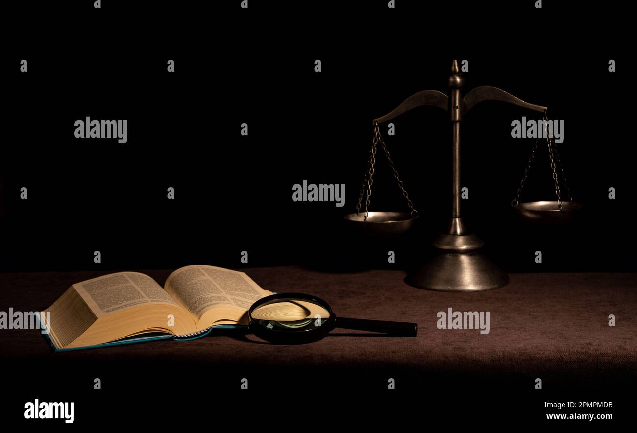 An antique-style metal balance scale, an open book and a magnifier ...