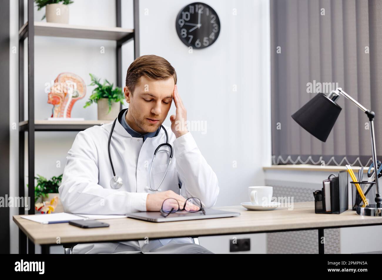 Handsome doctor man wearing medical uniform sitting on his workplace ...