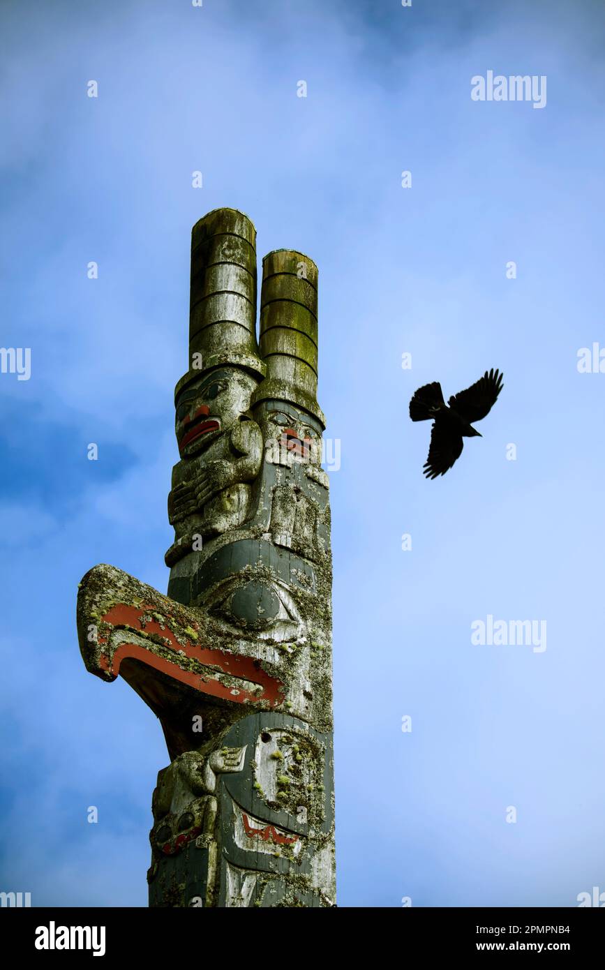 Top part of a totem pole with a crow flying in the background at Old ...