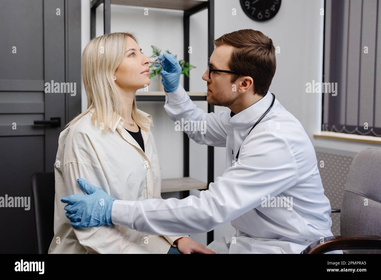 A young attractive otolaryngologist examining nose of a young patient ...