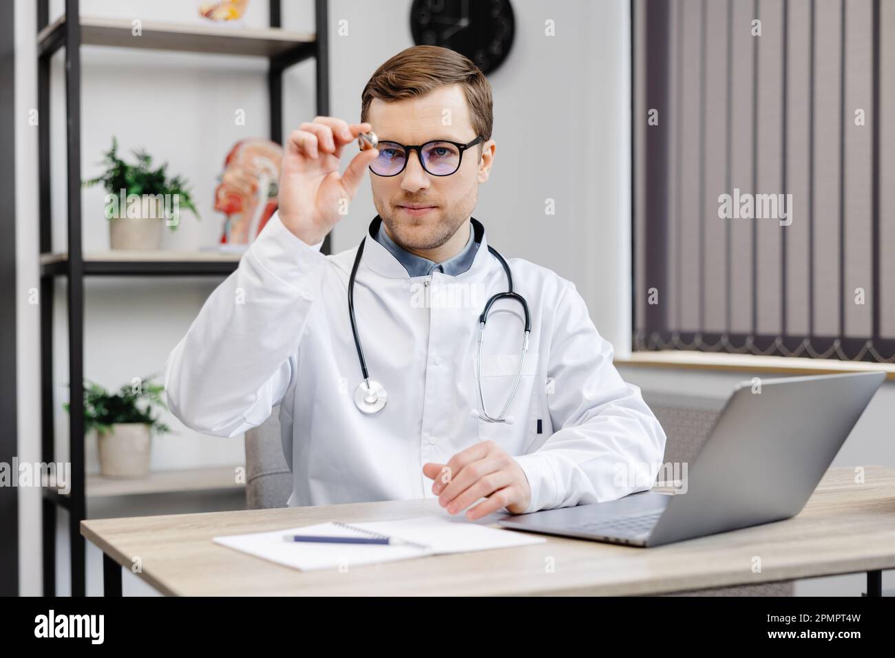 Young attractive doctor otolaryngologist sitting at his workplace in ...