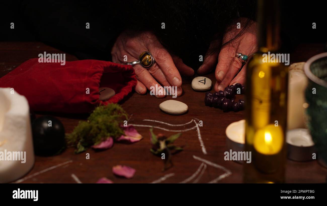 The hands of a woman drawing runes out of a small red bag. She is doing ...