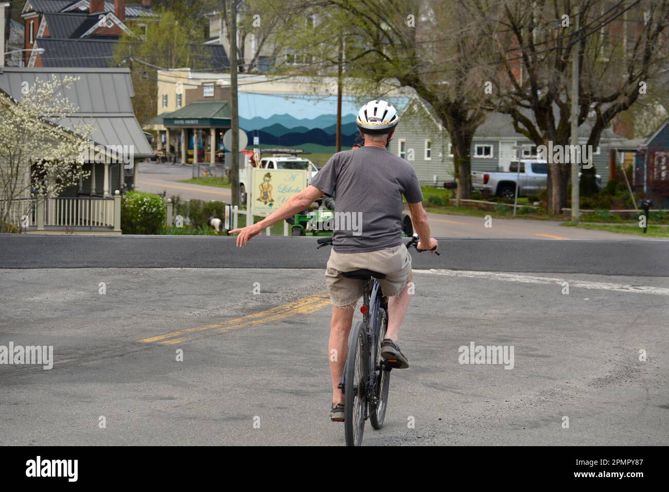 A senior man riding a bicycle signals a left turn as he rides along a ...