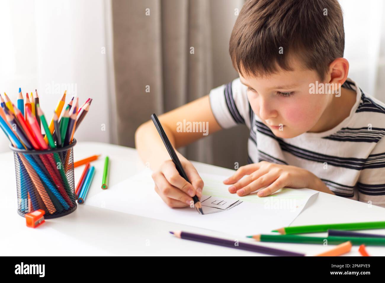 A child boy draws on white paper with colored pencils while sitting at ...