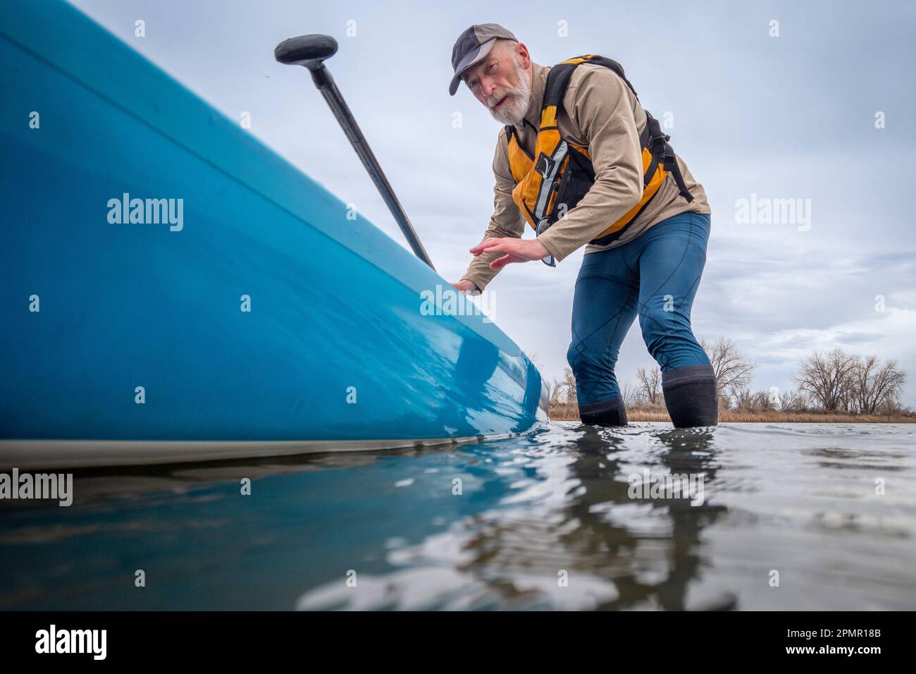senior male paddling a stand up paddleboard on a lake in early spring ...