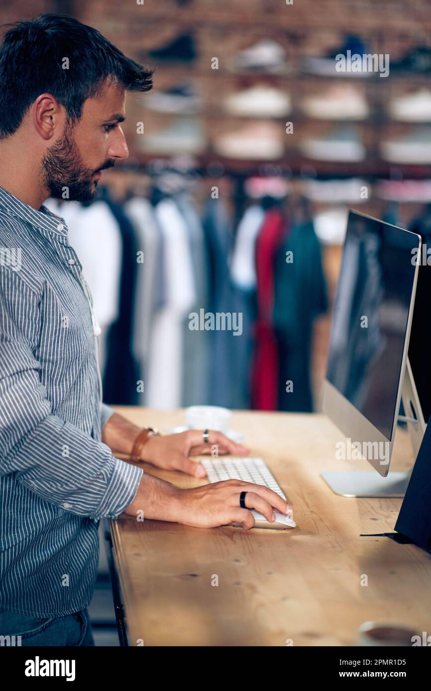 Young man standing at desk in a clothing shop, seraching through ...