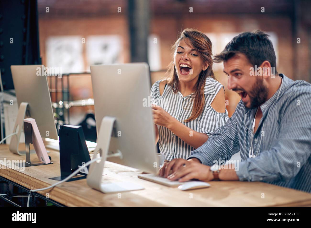 Joyful young colleagues working and looking at computer screen together ...