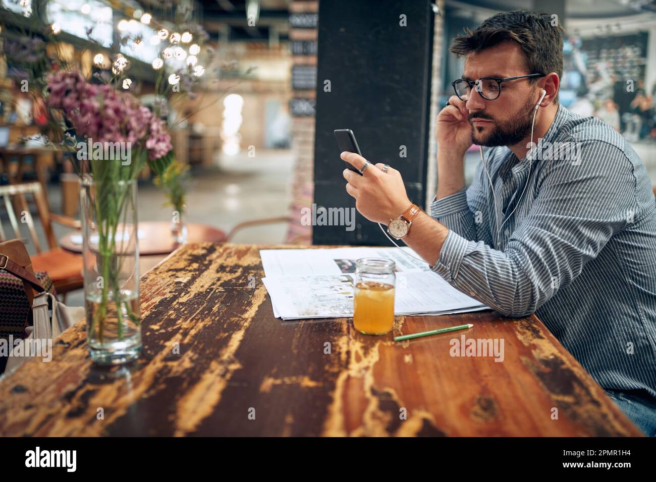 Man in casual wear, sitting in cafe alone, using phone, listening with ...