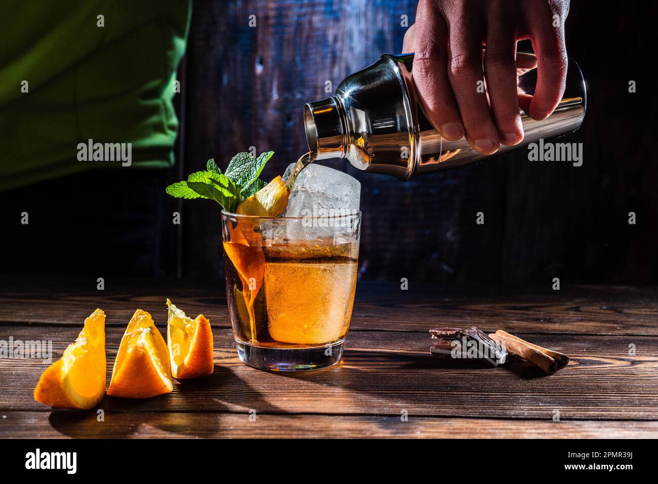 The bartender pours a drink from a shaker. Drink with ice and orange ...