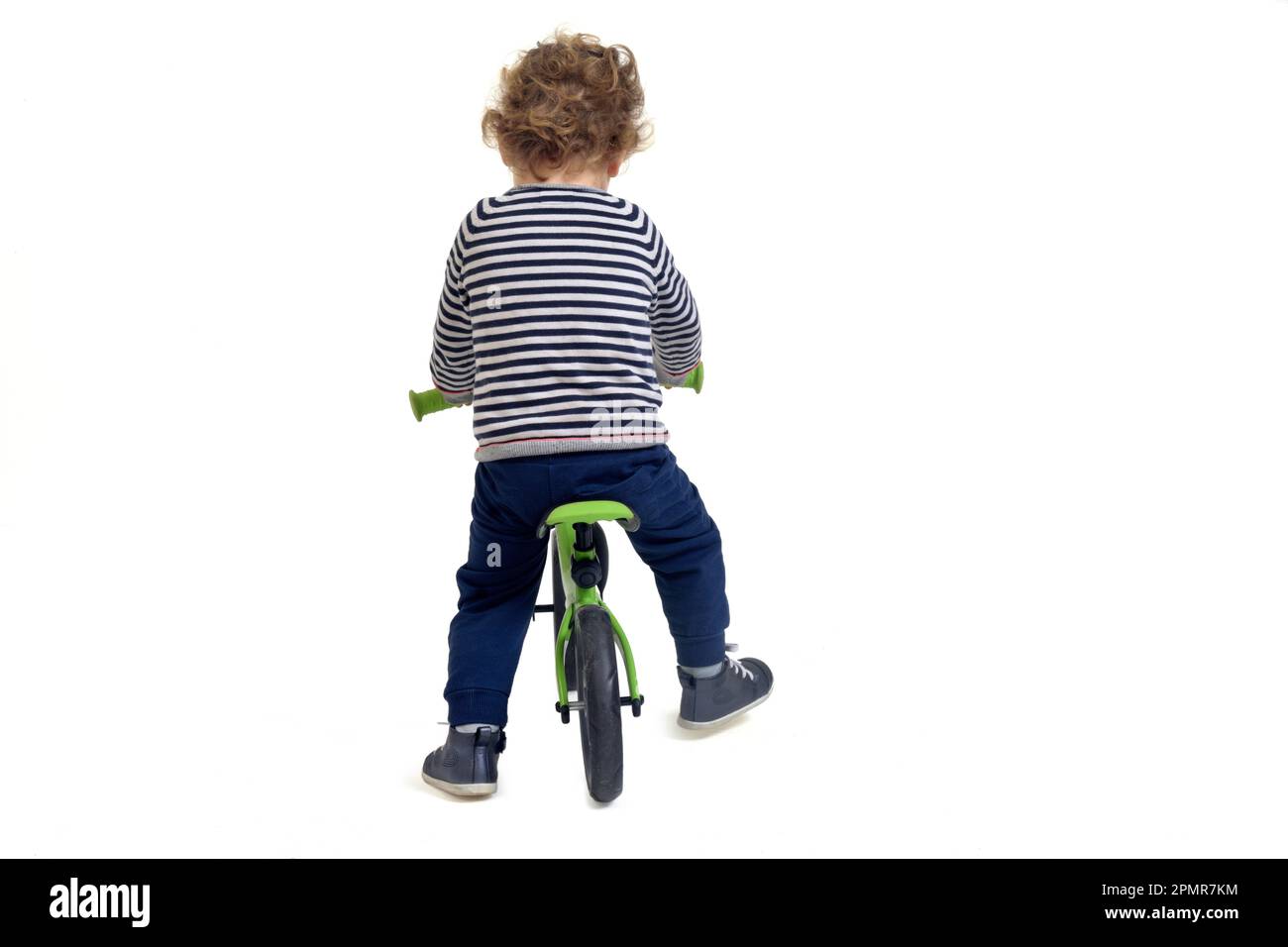 back view of a baby boy playing with a bicycle on white background ...