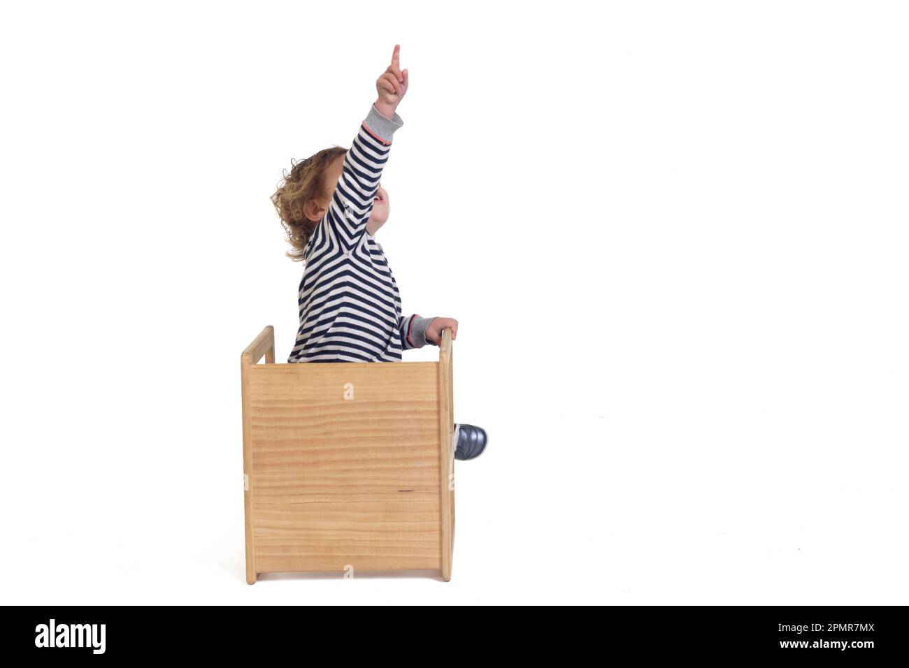 side view of a baby boy sitting on chair and pointing up on white ...