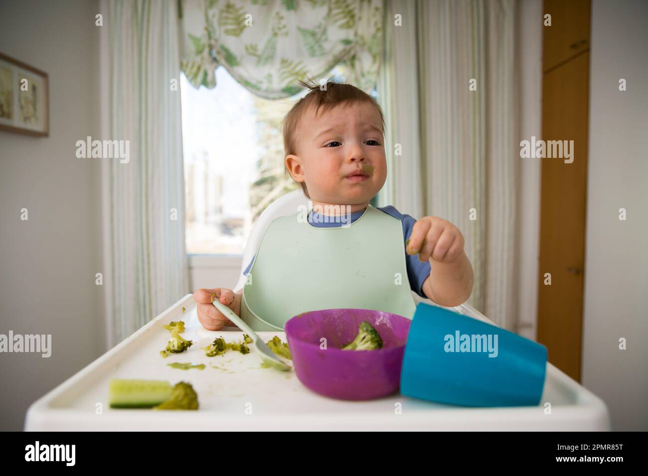 Cute baby eating with first solid food, infant sitting in high chair ...