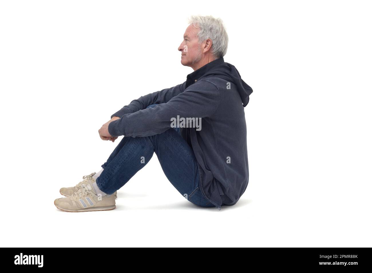 man sitting on the floor with legs folded and looking at away on white ...