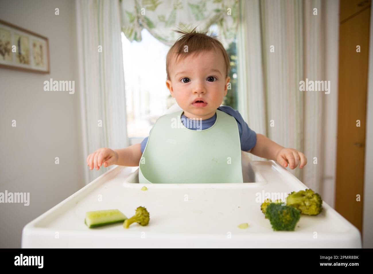 Cute baby eating first solid food, infant sitting in high chair. Child ...