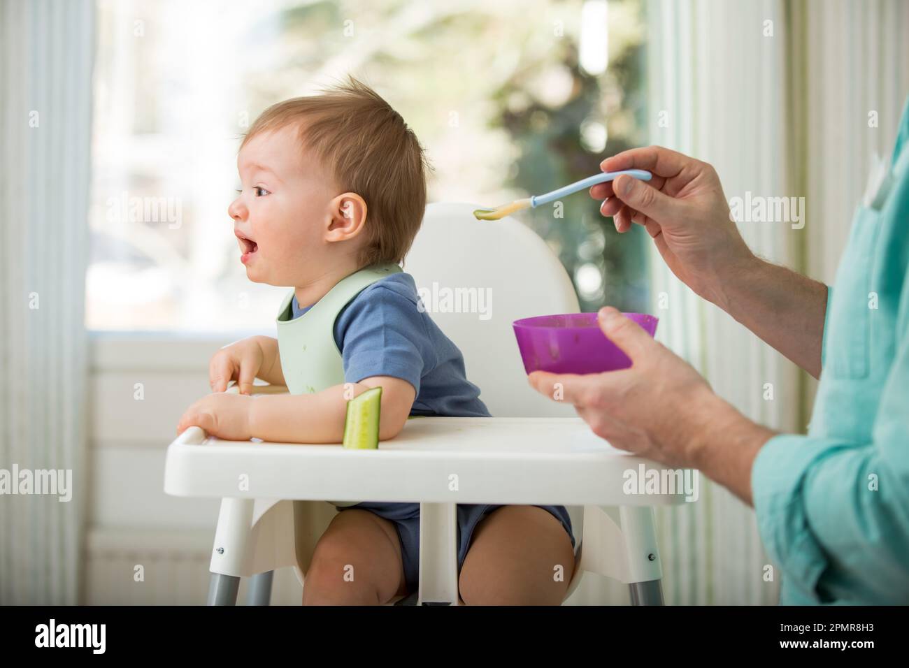 Father feeding his cute baby with first solid food, infant sitting in ...