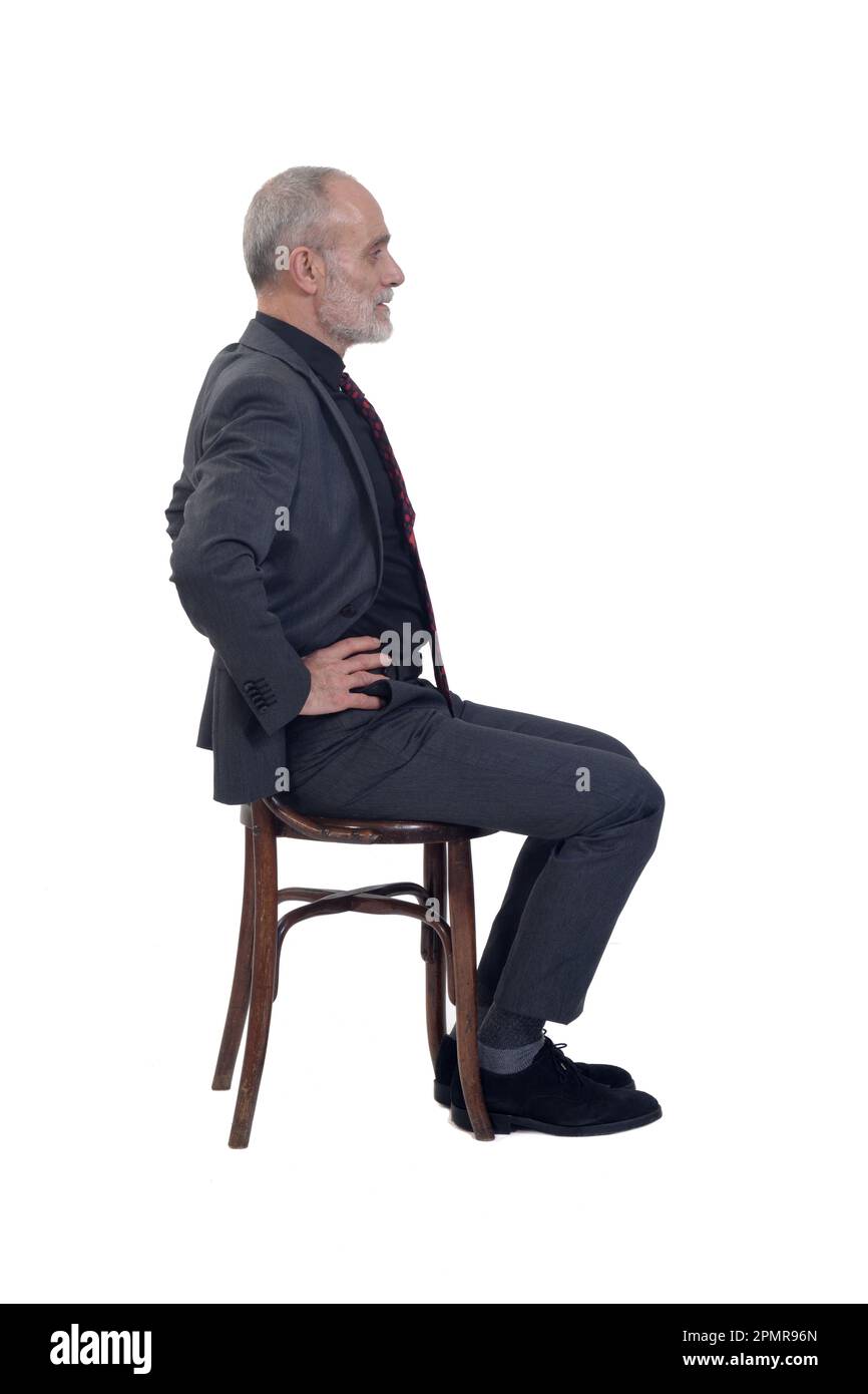side view of a man sitting on chair with suit and tie and arms akimbo ...