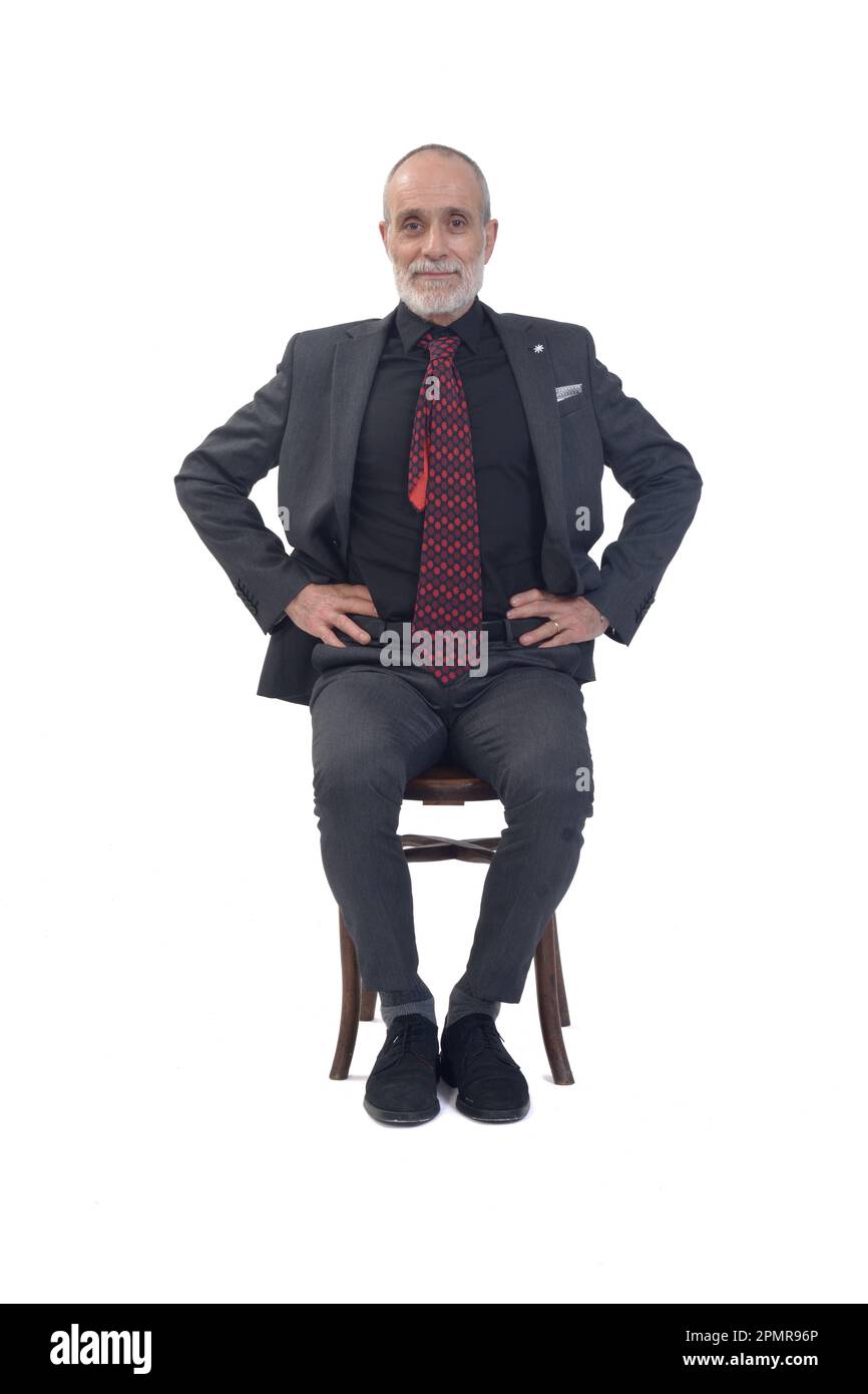 front view of a man sitting on chair with suit and tie and arms akimbo ...