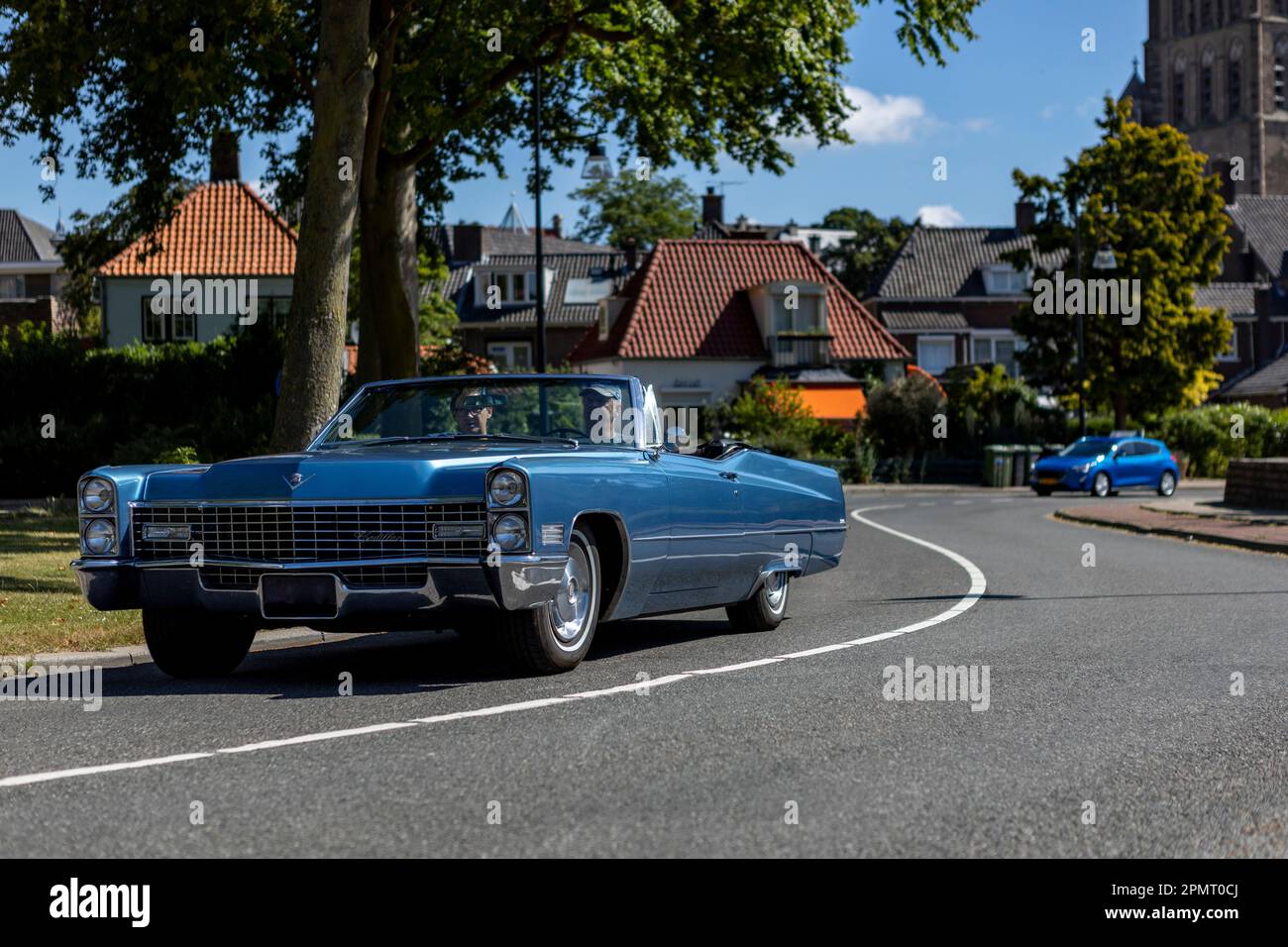 Vintage old timer car driving in a road curve with historic tower town ...