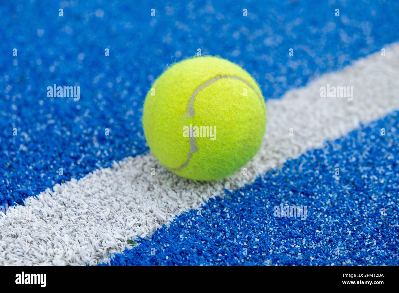 A close-up of a bright blue tennis court featuring a single tennis ball ...