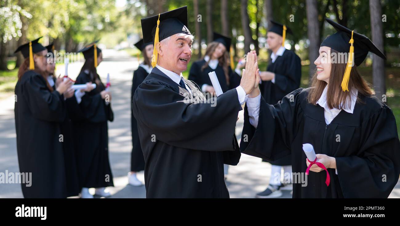 A group of graduates in robes outdoors. An elderly man and a young ...