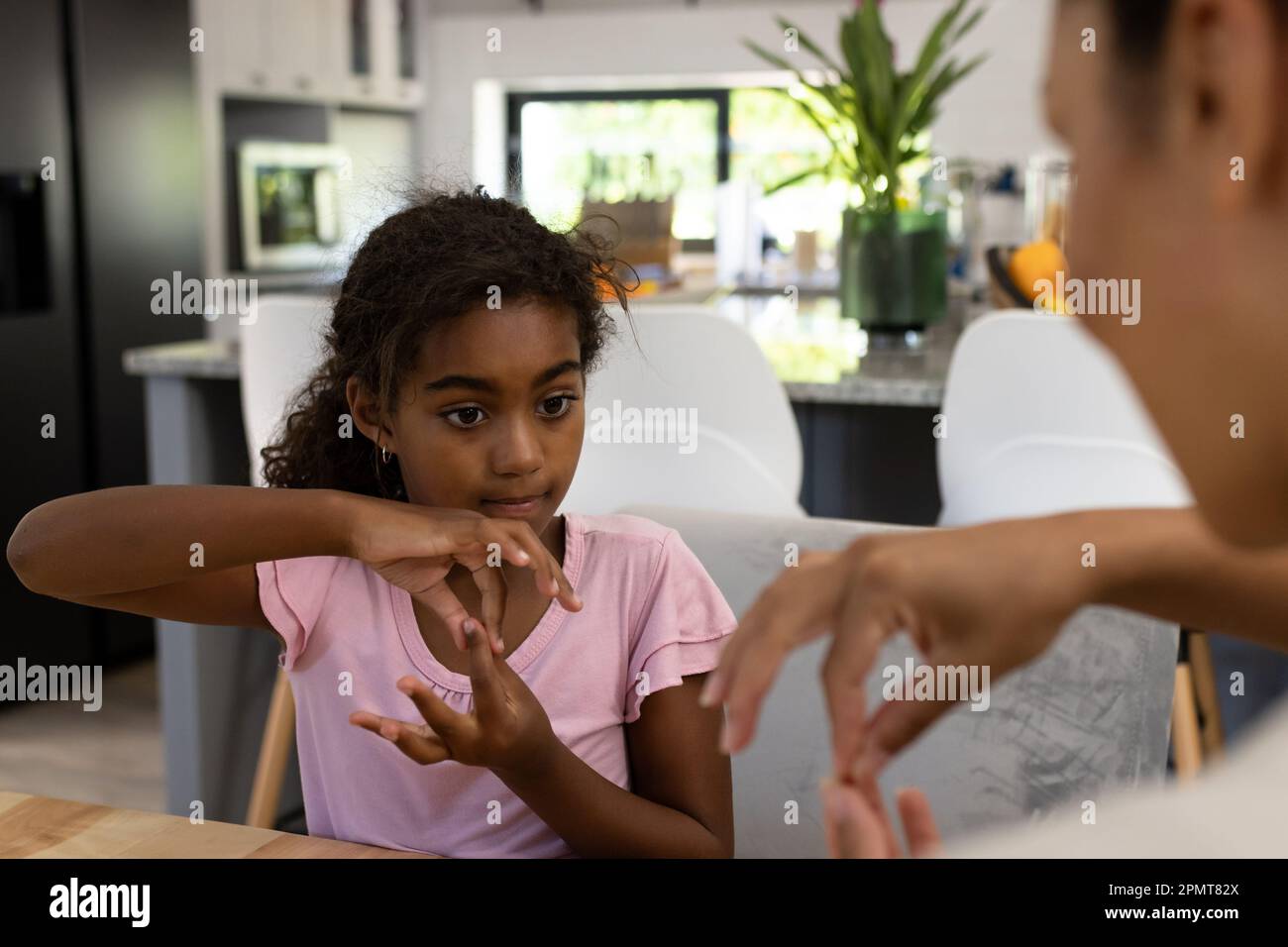 Focused biracial mother sitting at table teaching her daughter sign ...
