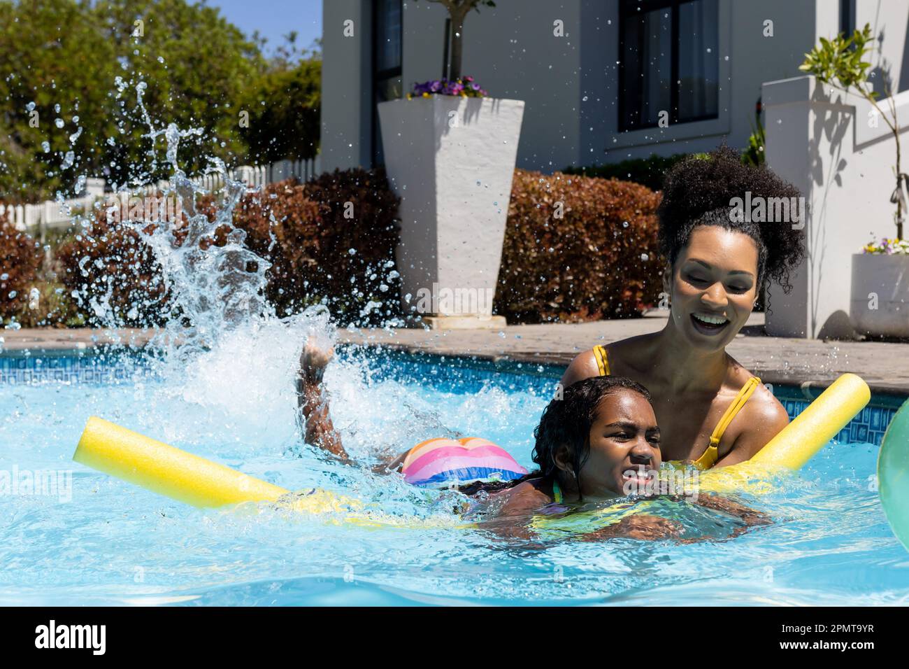 Happy biracial mother and daughter learning to swim with float in ...