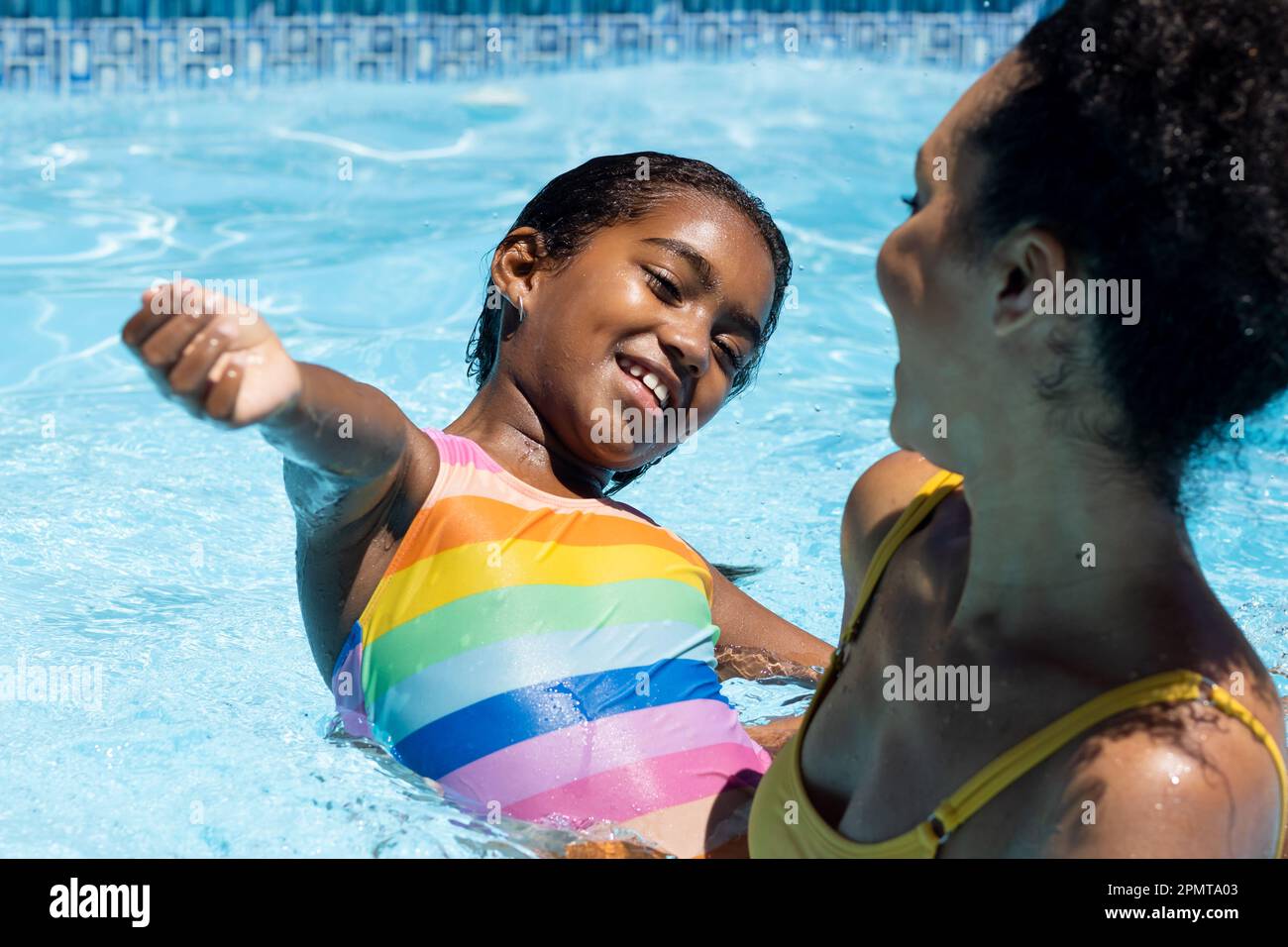 Happy biracial mother and daughter playing in sunny outdoor swimming ...