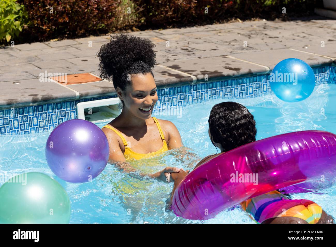 Happy Biracial Mother And Daughter Playing With Inflatable In Sunny