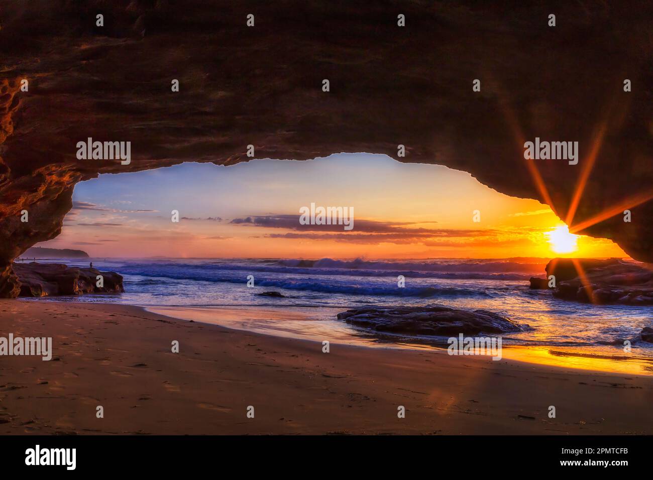 Sun rays over Pacific ocean horizon from inside eroded beach on Caves ...