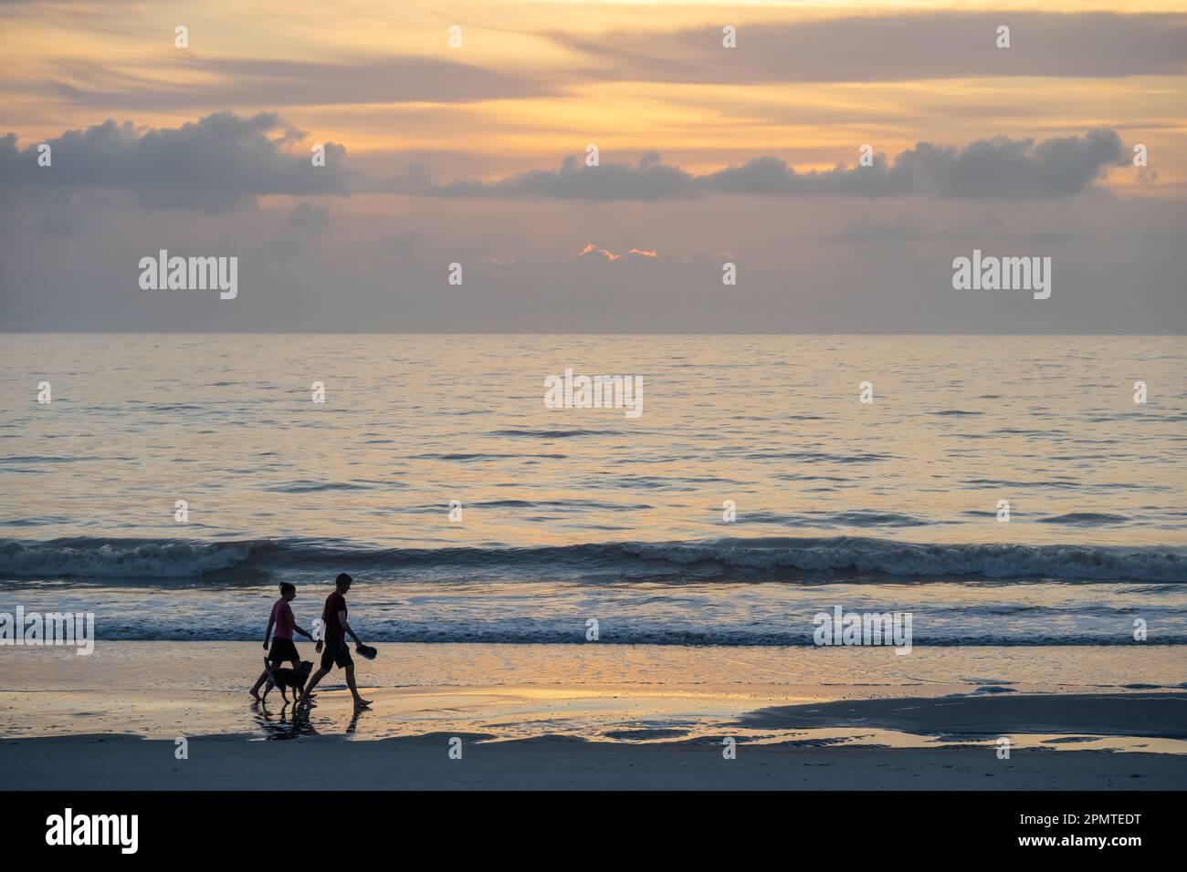 Couple taking a sunrise stroll with their dog along the shoreline at ...