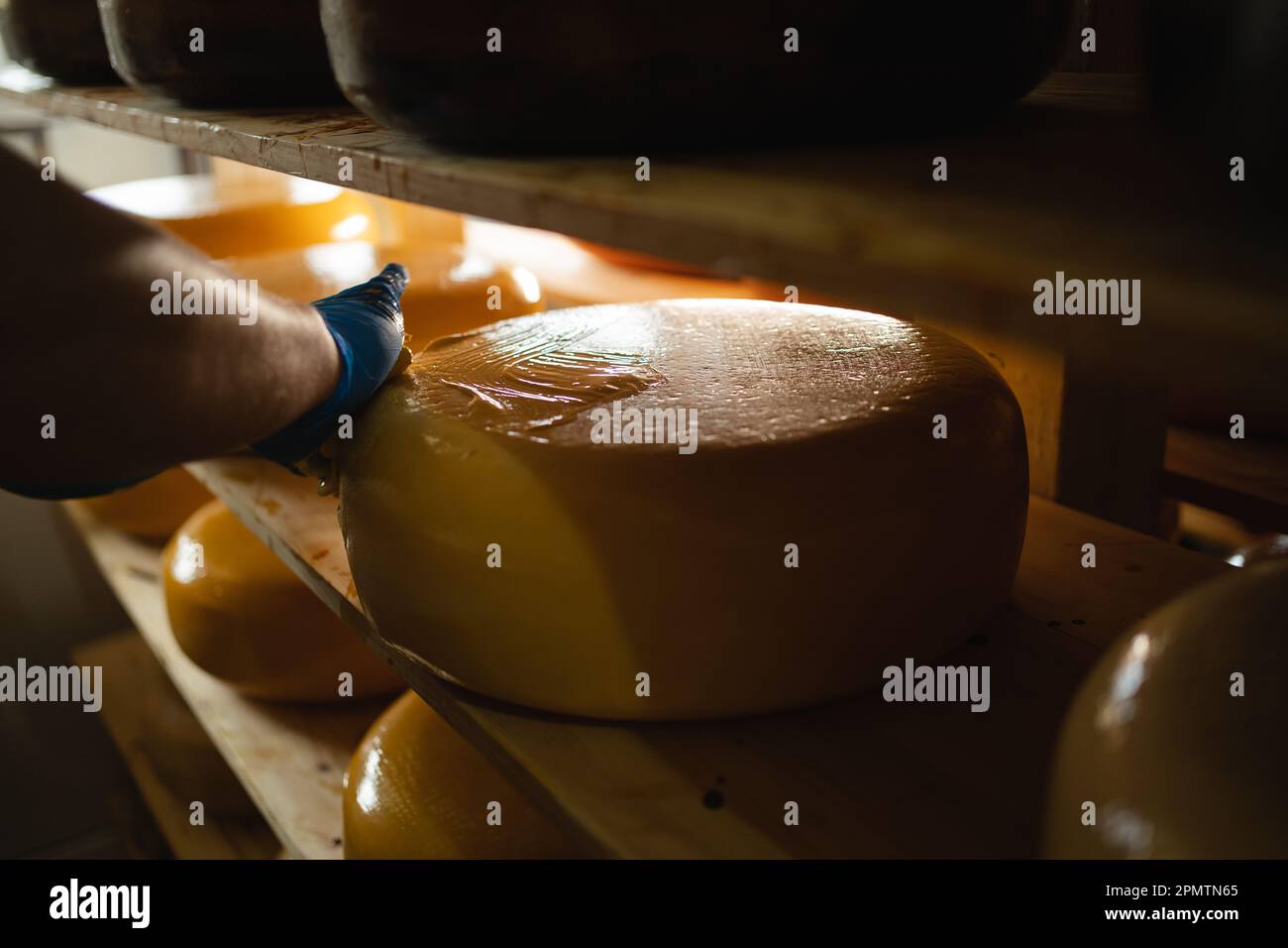Close up of male worker coating cheese with wax in factory warehouse ...