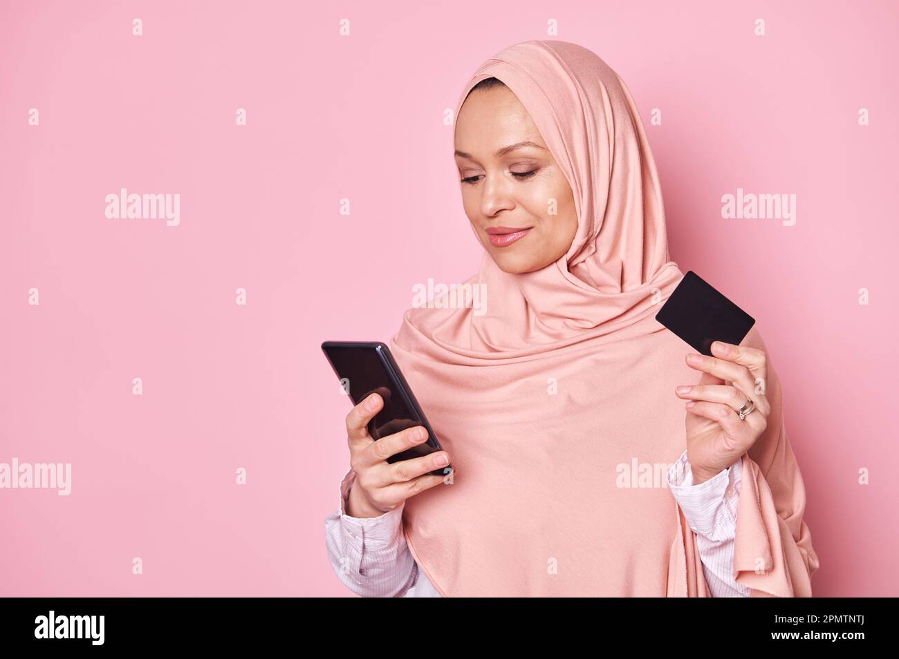 Beautiful Arabic Muslim woman in pink hijab, using smartphone, holding ...